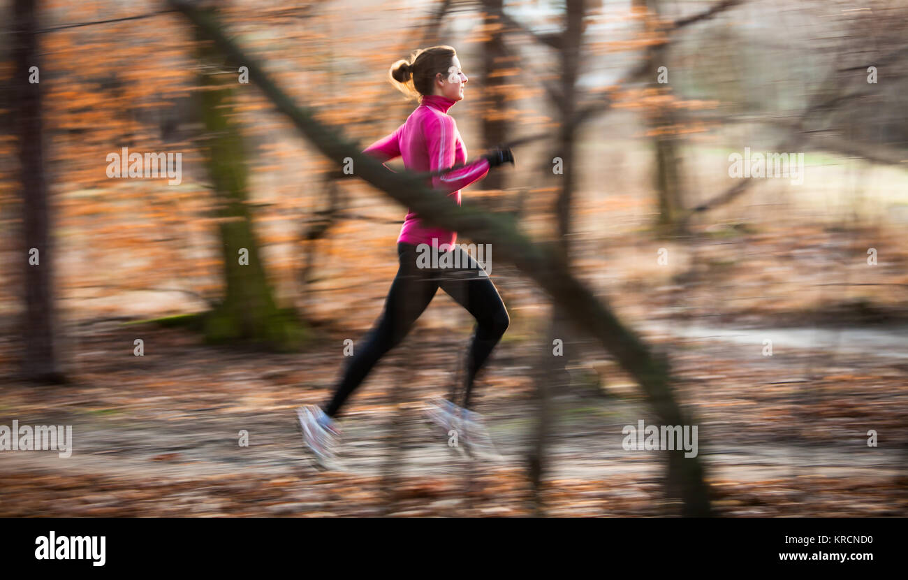 Young woman running outdoors in a city park on a cold fall/winter day ...