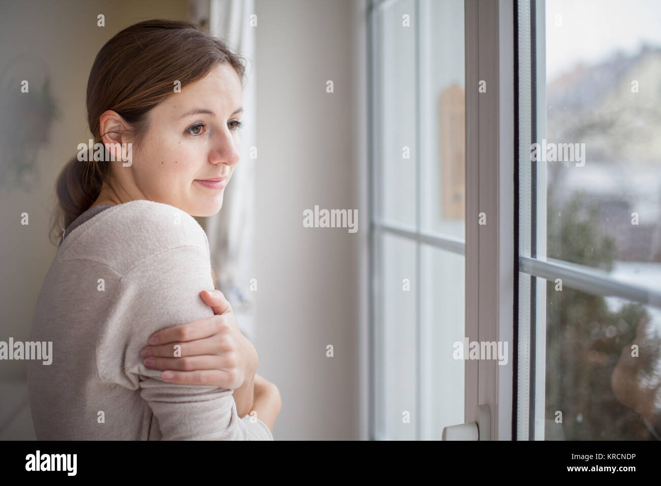 Woman looking from a window of her house on a cold and snowy winter day ...
