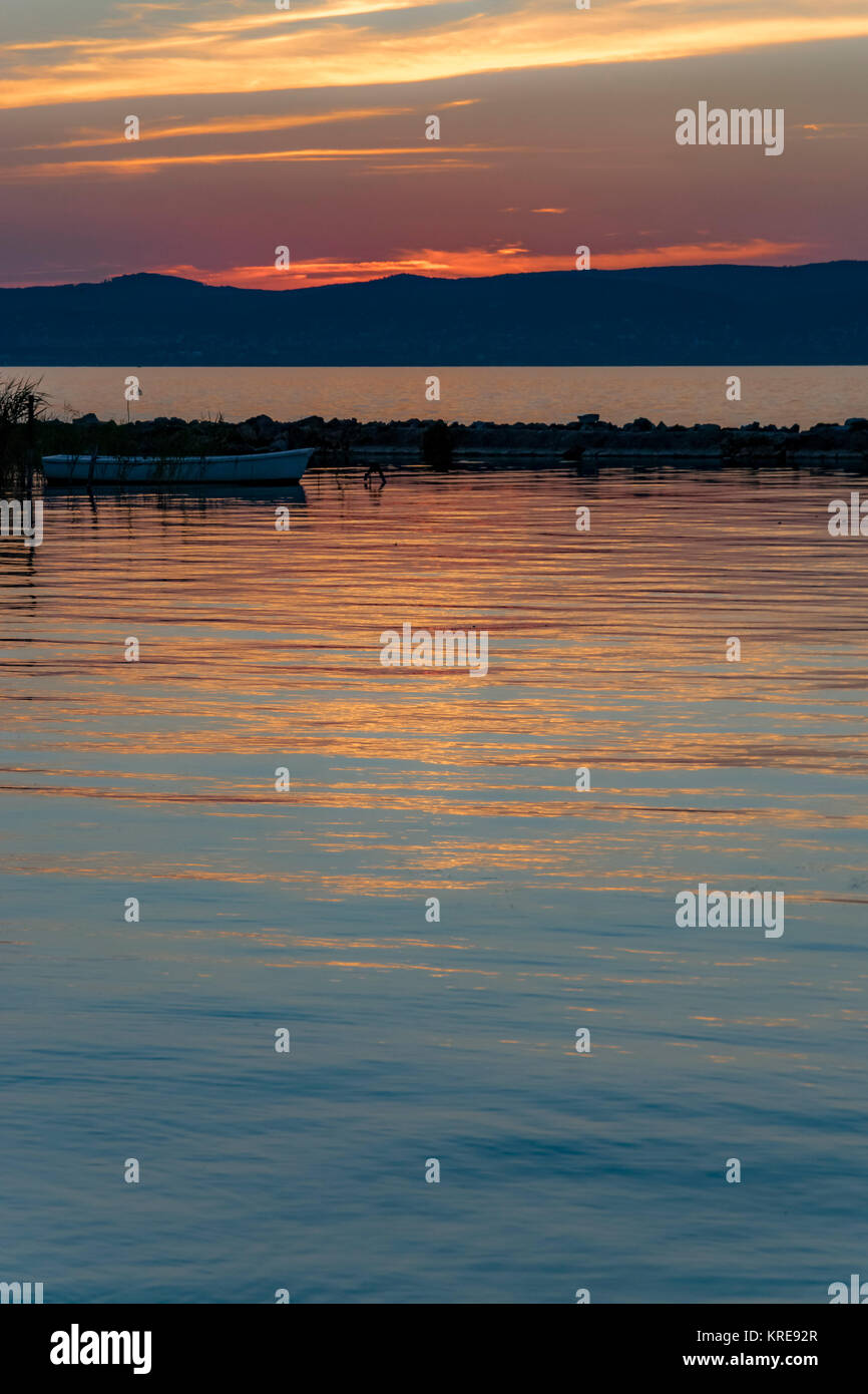 Scenic view of vivid sunset reflection on calm water, silhouette of ...