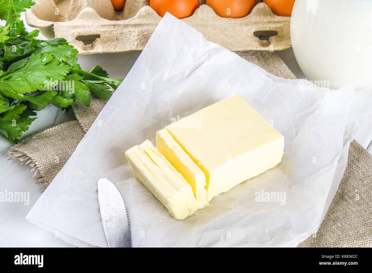 A bar of butter is cut into pieces on a wooden board with a knife ...