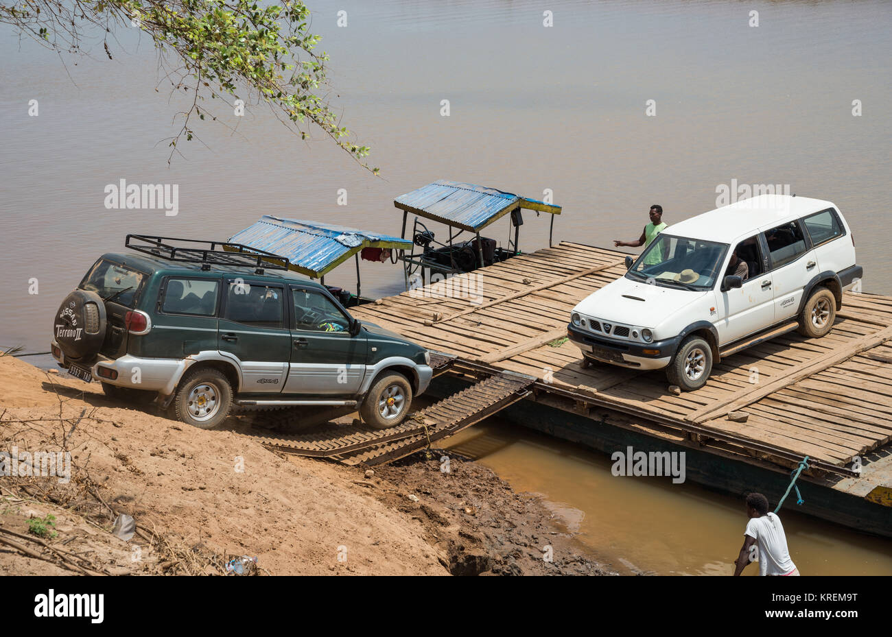 A green SUV driving on board a ferry boat to cross Mania River ...