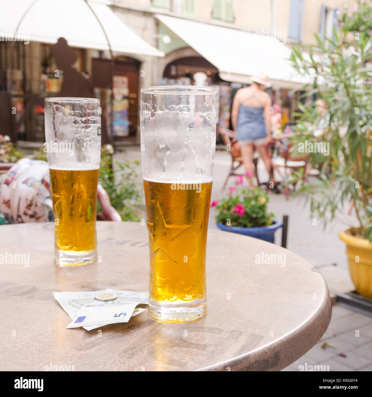 Two glasses full of beer stand on a table in a street cafe with bills ...