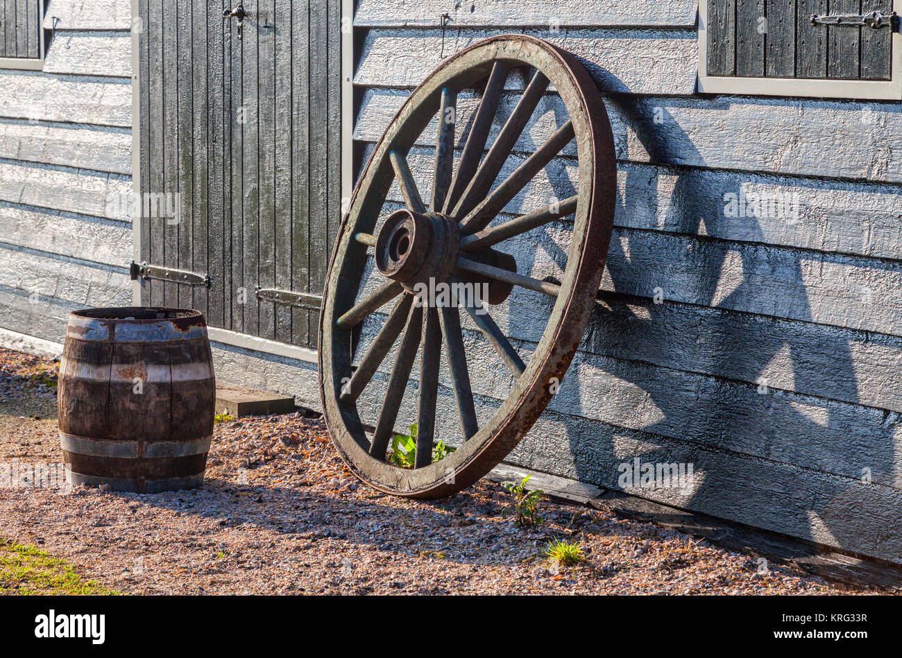 Image of a rusty old wheel and a barrel near a the wall of a barn Stock ...