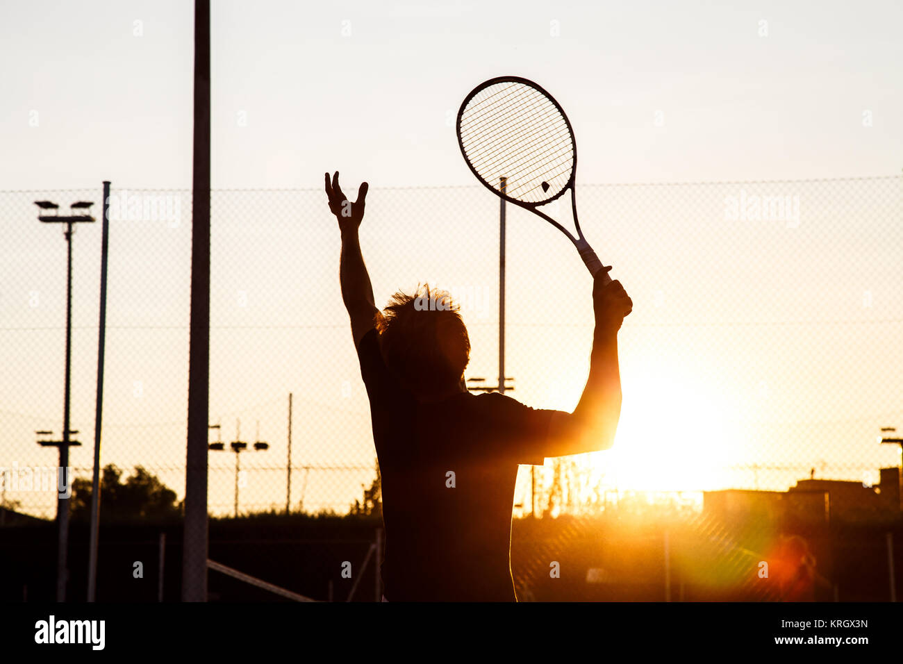 Back view of sportsman with tennis racket hitting ball in back light on ...