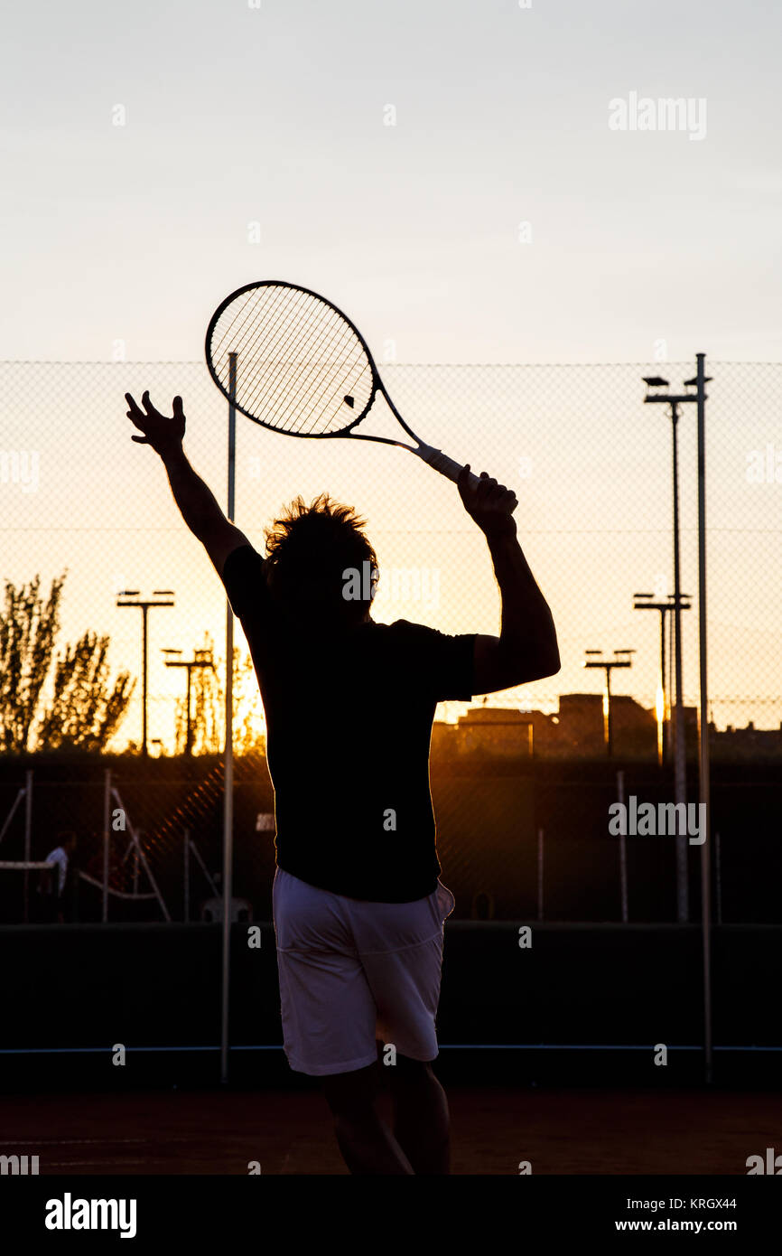 Back view of sportsman with tennis racket hitting ball in back light on ...