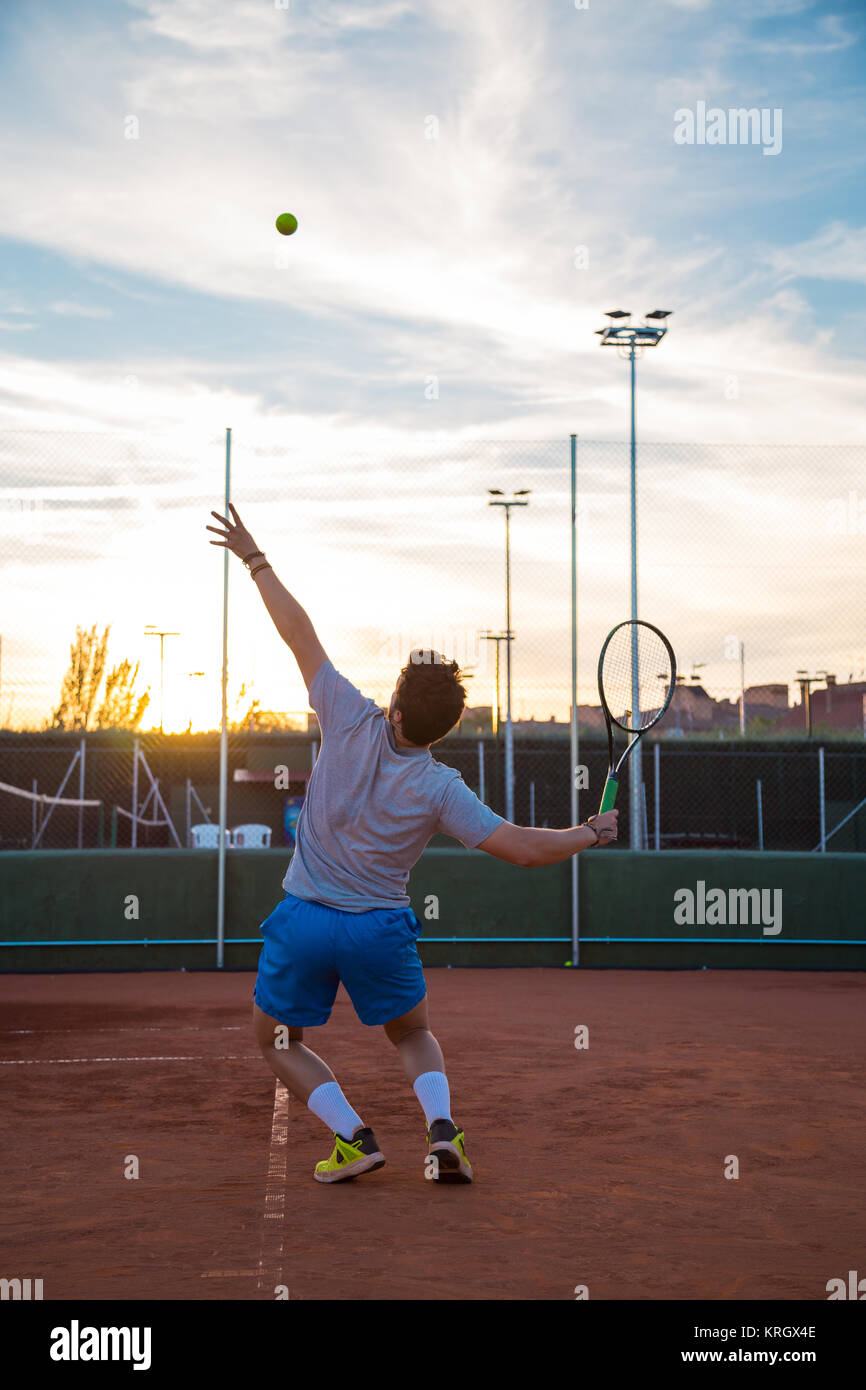 Back view of sportsman with tennis racket hitting ball in back light on ...
