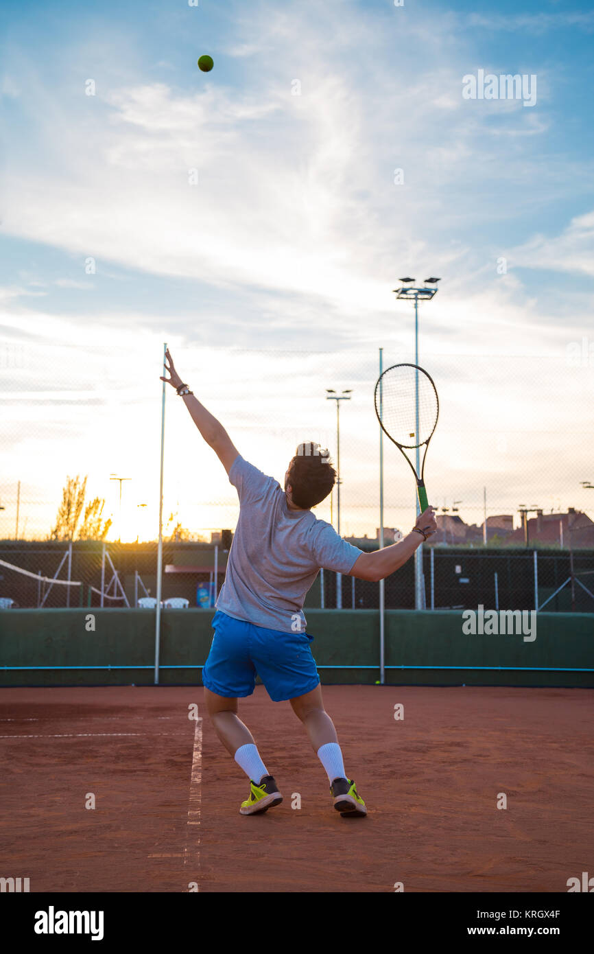 Back view of sportsman with tennis racket hitting ball in back light on ...