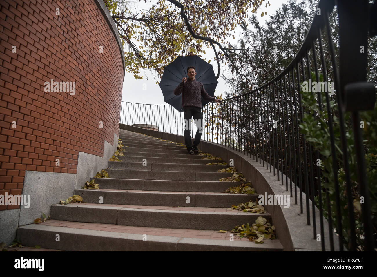 Young man with umbrella walking downstairs in park in rainy day Stock ...