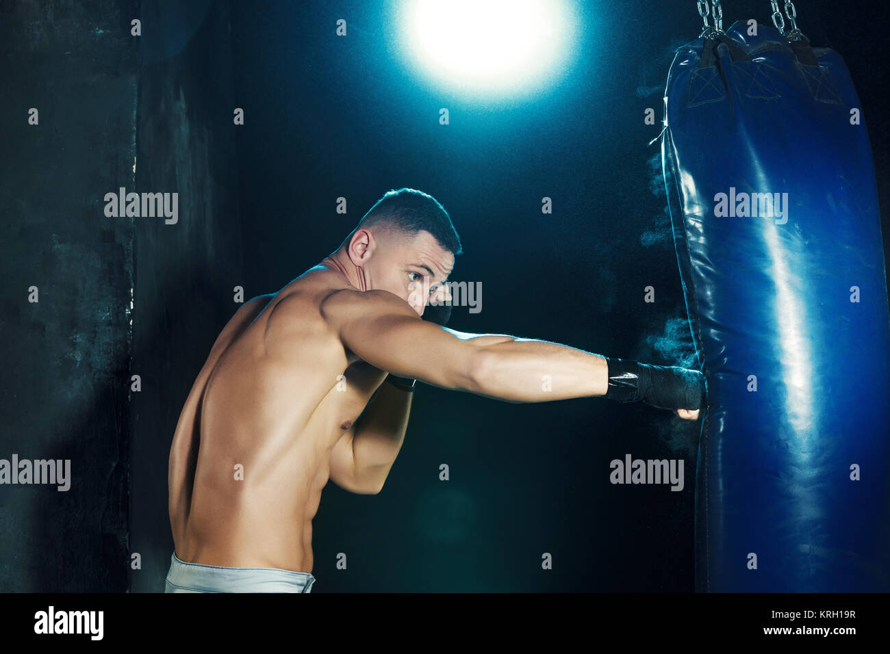 Male boxer boxing in punching bag with dramatic edgy lighting in a dark ...