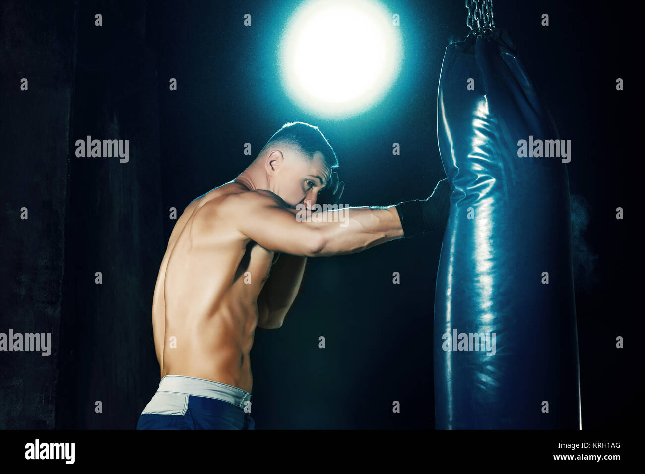 Male boxer boxing in punching bag with dramatic edgy lighting in a dark ...