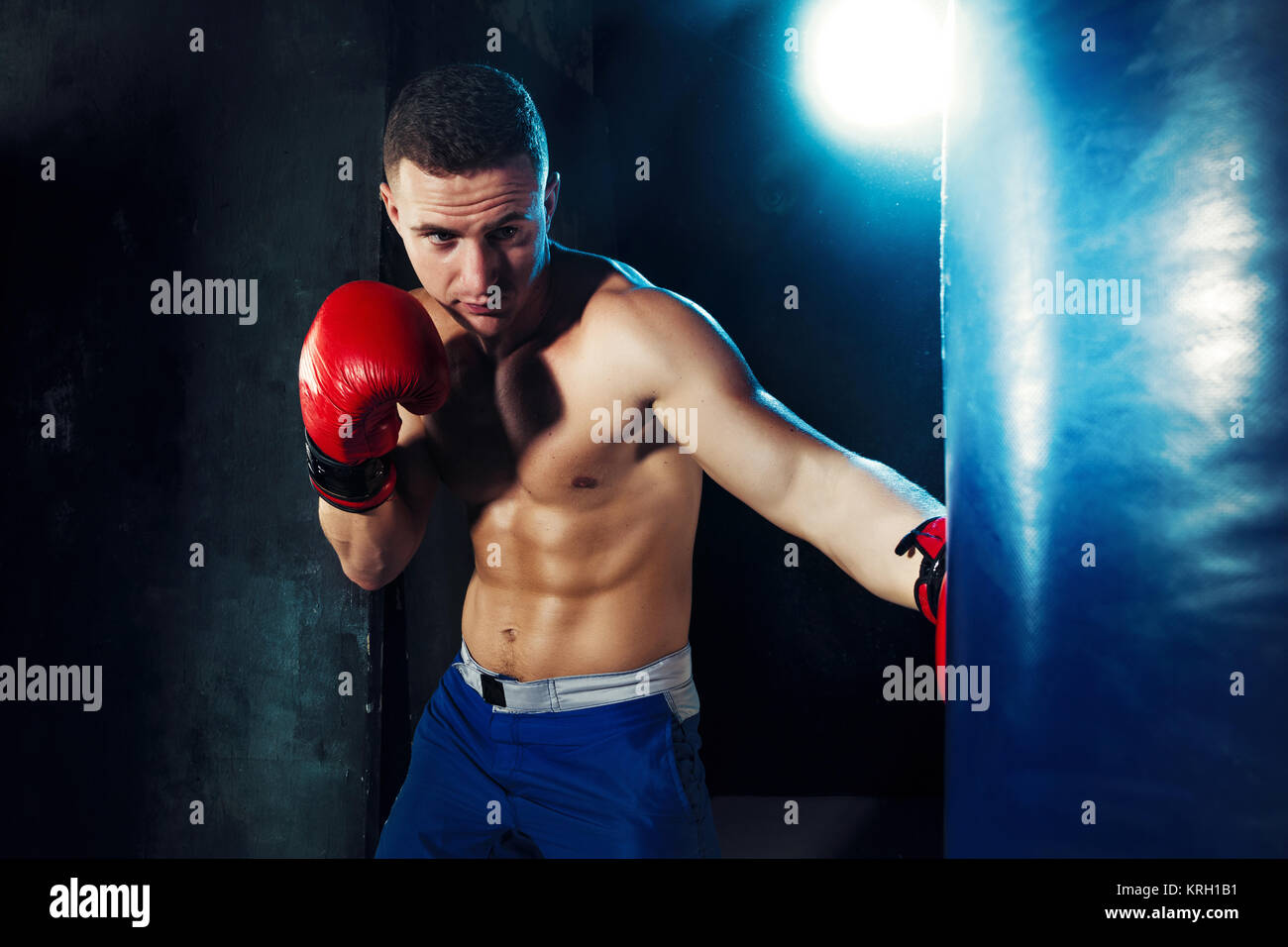 Male boxer boxing in punching bag with dramatic edgy lighting in a dark ...