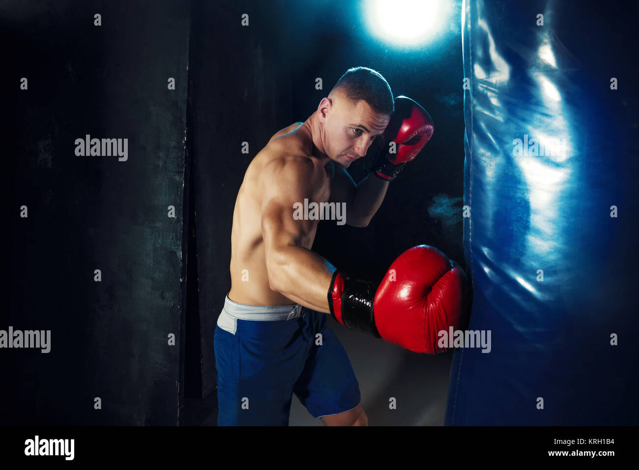 Male boxer boxing in punching bag with dramatic edgy lighting in a dark ...