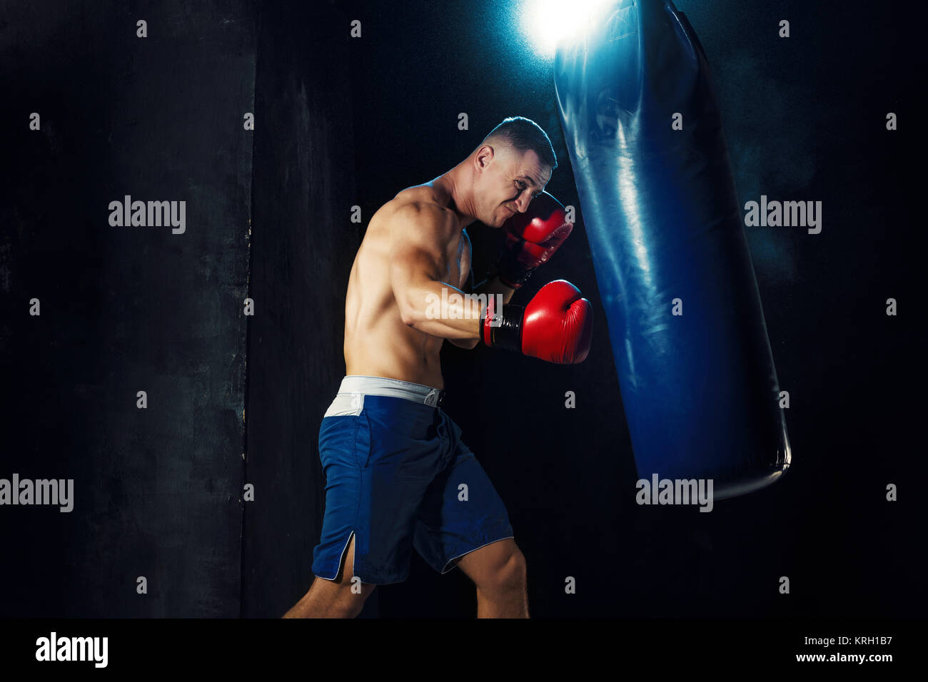 Male boxer boxing in punching bag with dramatic edgy lighting in a dark ...
