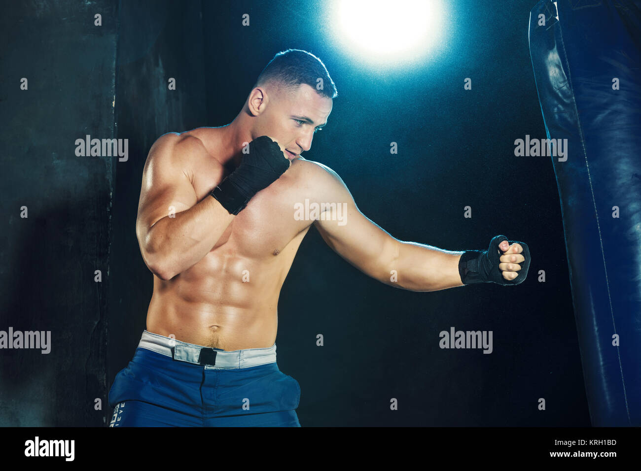 Male boxer boxing in punching bag with dramatic edgy lighting in a dark ...