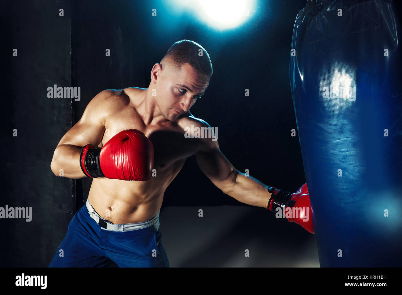 Male boxer boxing in punching bag with dramatic edgy lighting in a dark ...