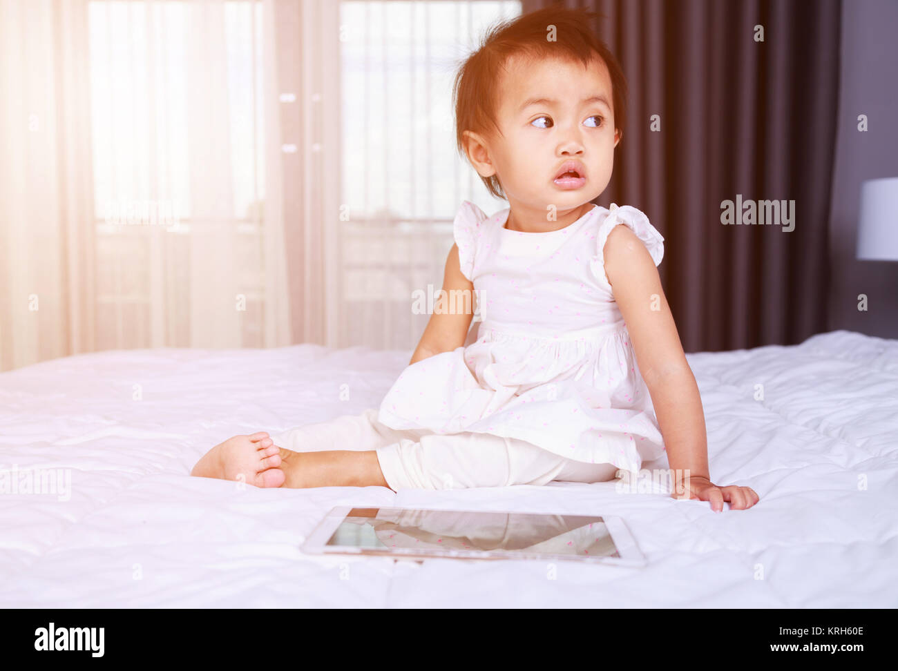 baby are looking to play and read tablet computer on bed at home Stock ...