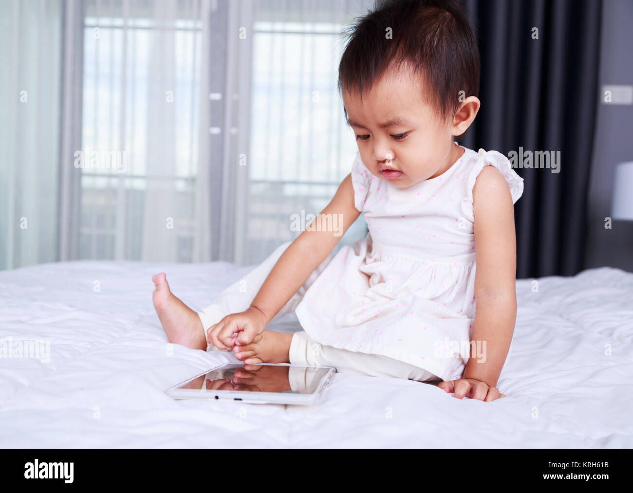 baby are looking to play and read tablet computer on bed at home Stock ...
