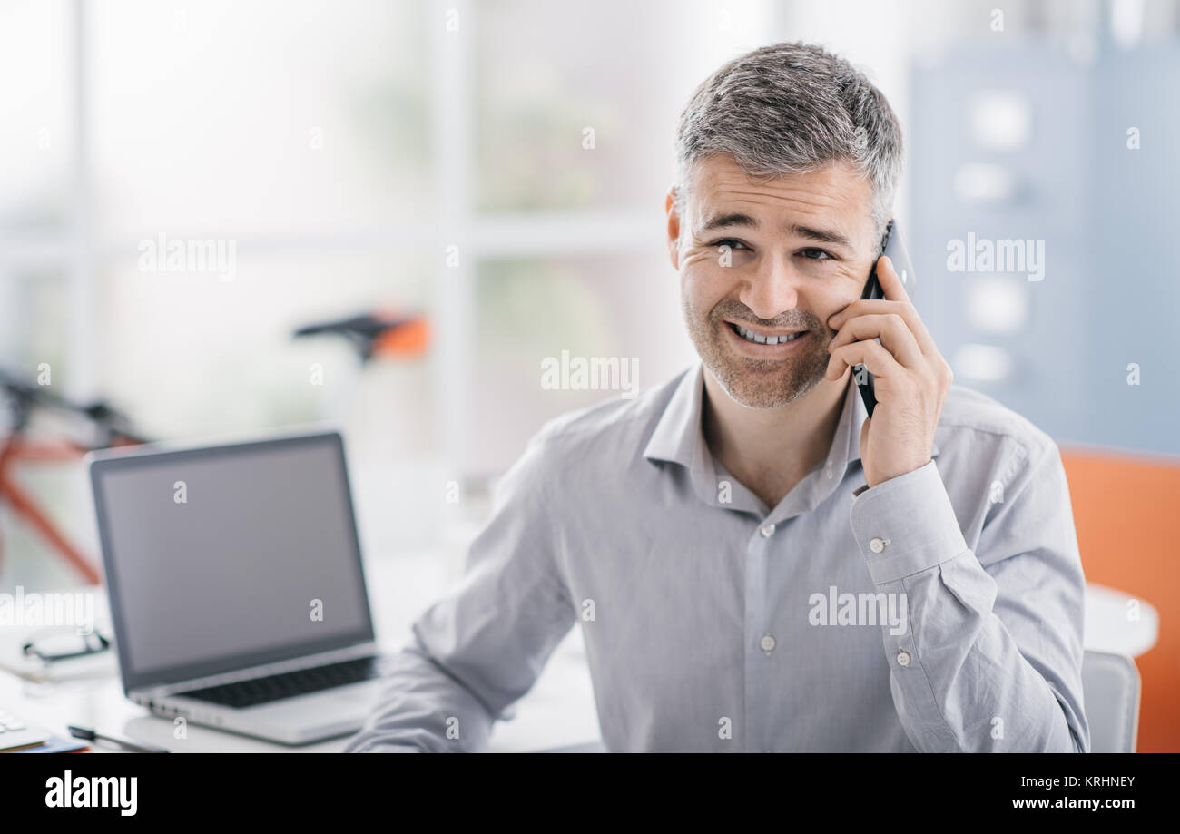 Professional smiling office worker sitting at desk and having a phone ...