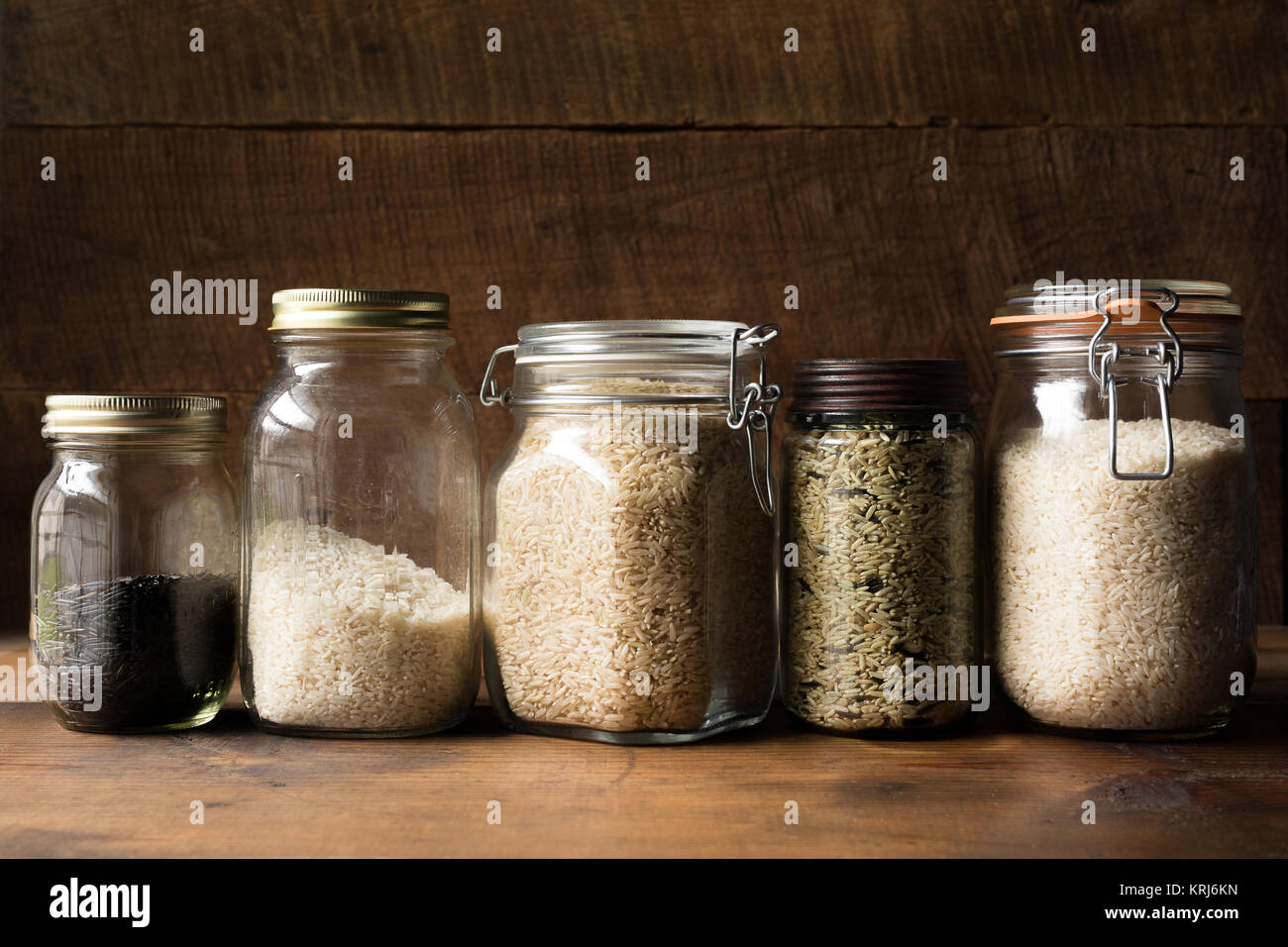 Several jars in a row filled with different types of dried rice. Wooden ...