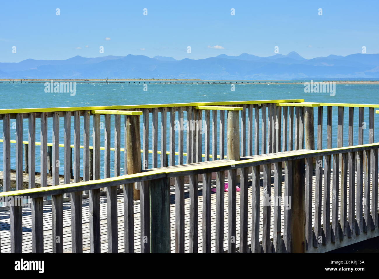 Wooden safety railing on jetty with sea and distant hills in background ...