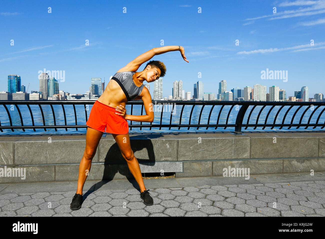 Mixed race woman stretching arm at waterfront Stock Photo - Alamy