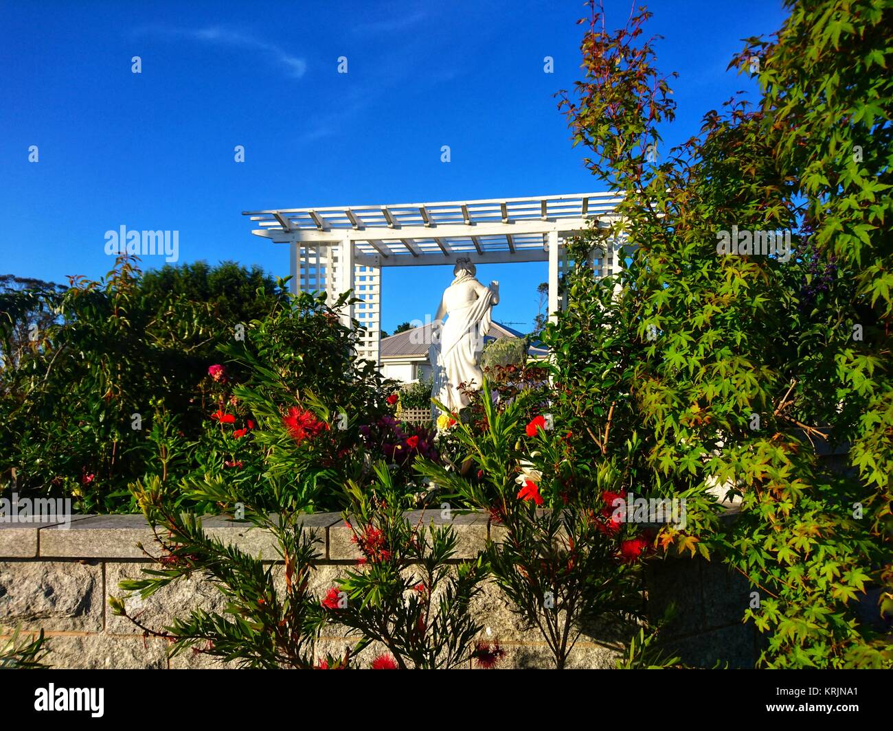 Female statue of Greek goddess under a wooden gazebo amid green bushes ...