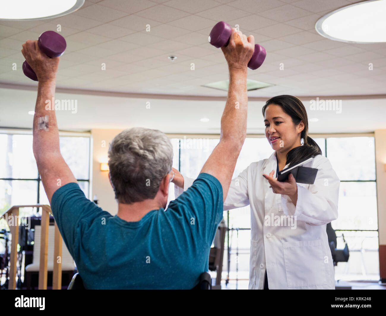 Physical therapist helping man lifting weights Stock Photo - Alamy
