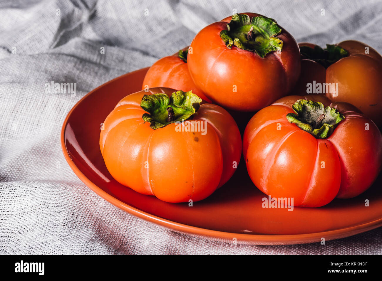 Persimmons on Orange Plate Stock Photo - Alamy