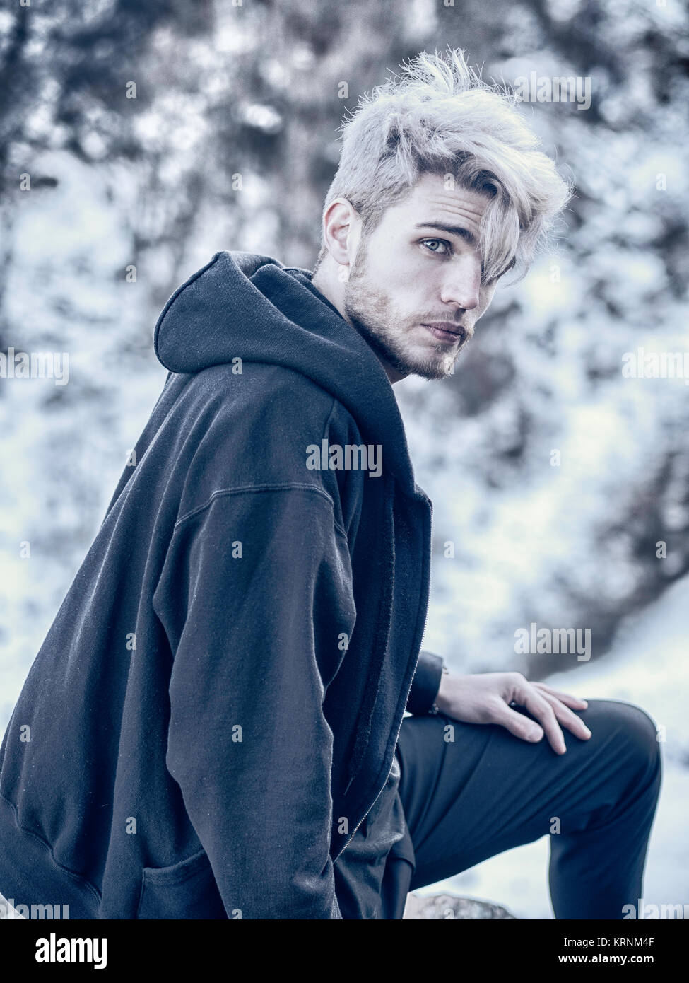 Portrait of young man in hoodie posing outdoor in winter setting with ...