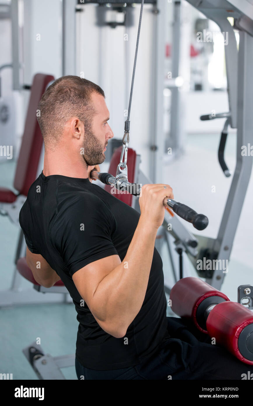 Determined young muscular man working on fitness machine at the gym ...