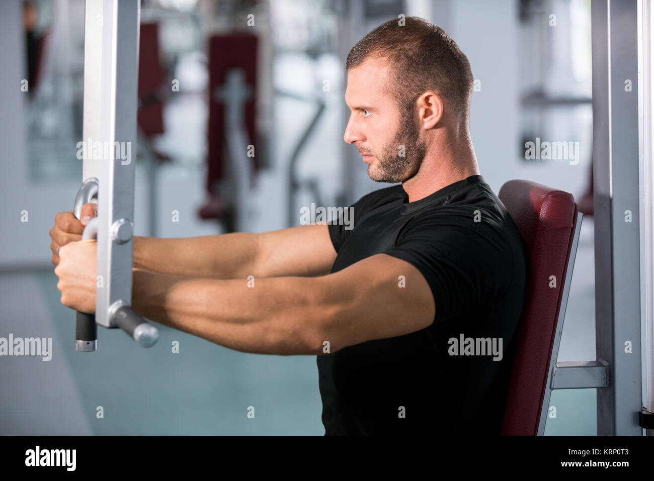 Determined young muscular man working on fitness machine at the gym ...