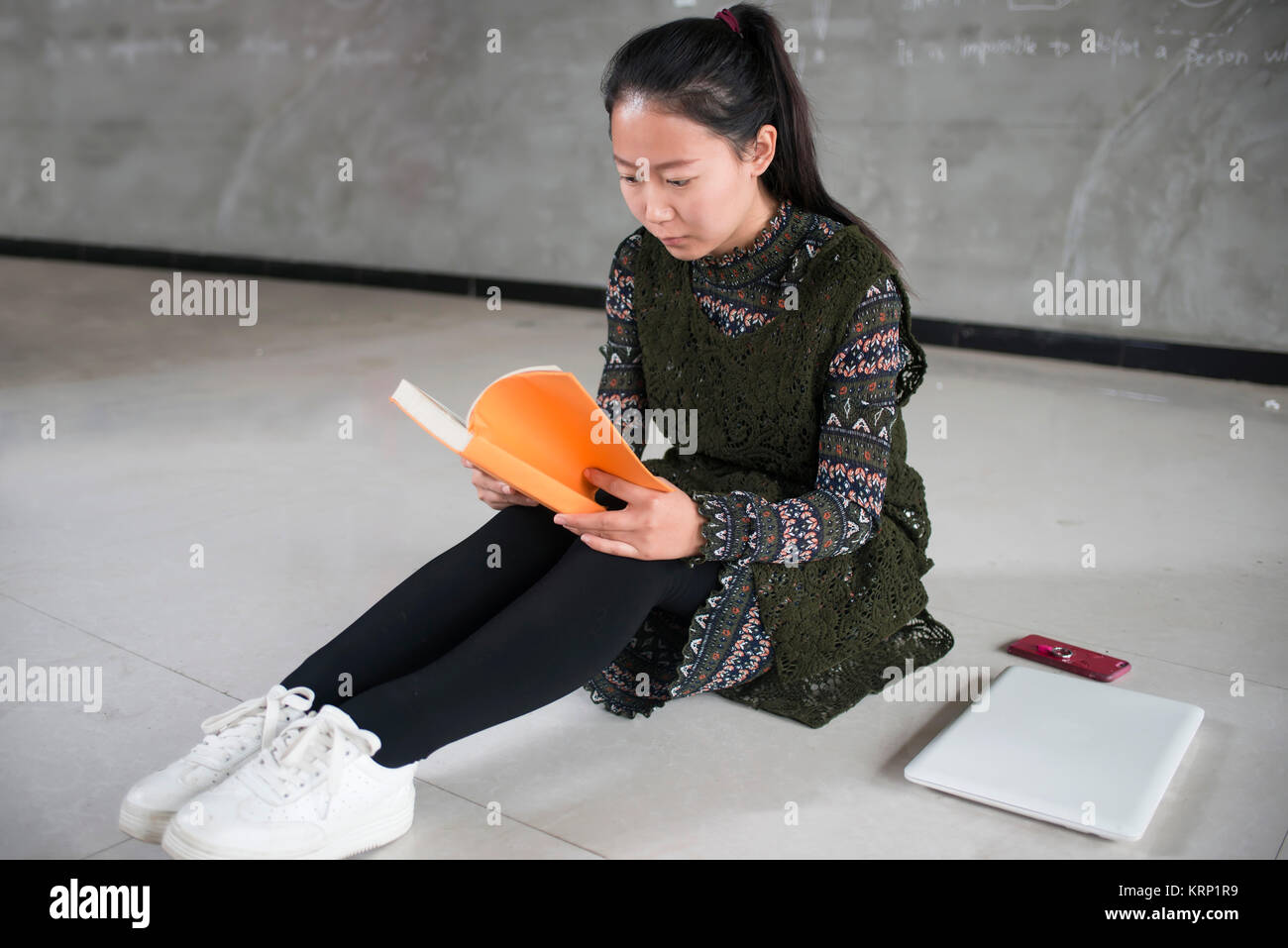 Young student sitting on floor in a classroom and reading a book Stock ...