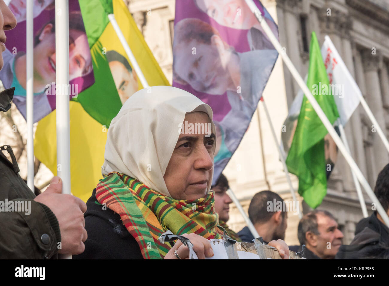 A woman in a headscarf and Kurdish scarf holds a banner at the protest ...