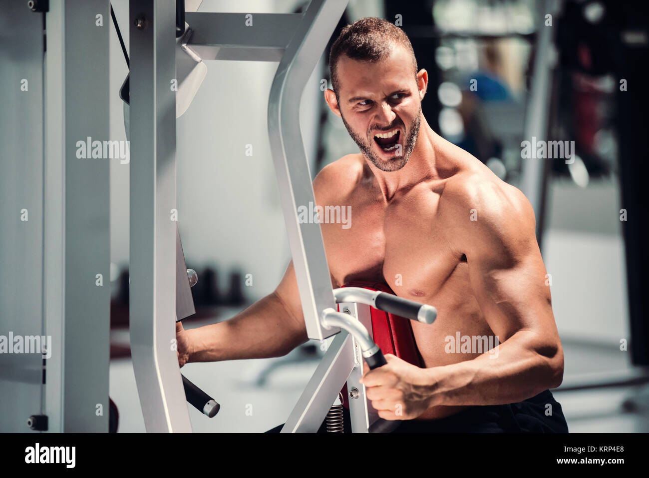 Determined young muscular man working on fitness machine at the gym ...