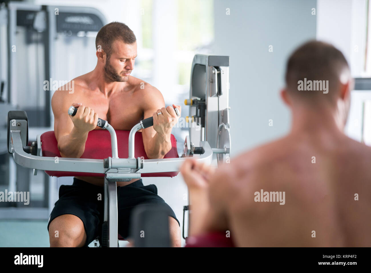 Determined young muscular man working on fitness machine at the gym ...