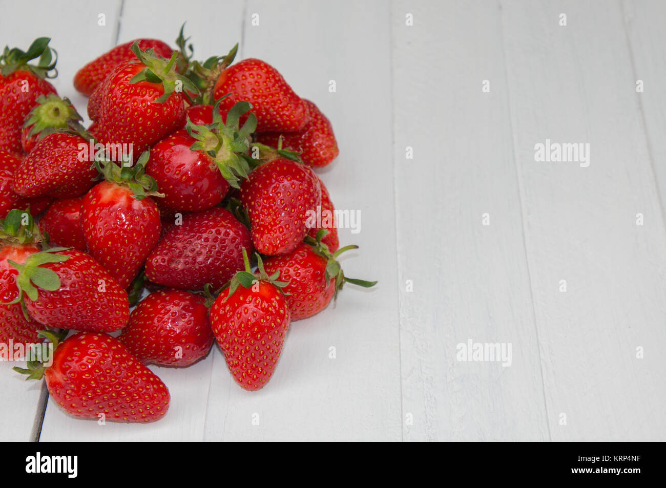 pile of ripe red strawberries on a white surface, empty space on the ...