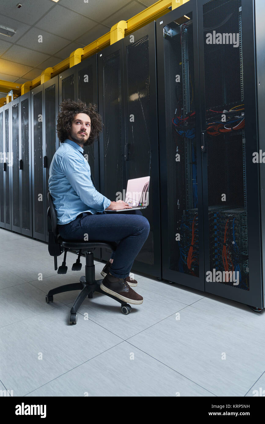 Young technician working on a laptop next to black server racks Stock ...