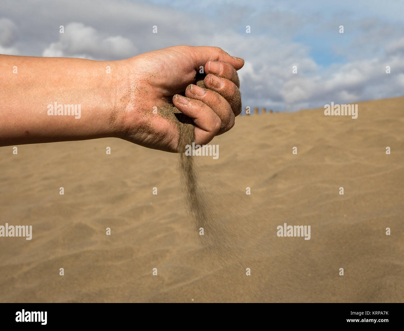 Female hand with sand against the Dunes of Maspalomas with blue sky and ...
