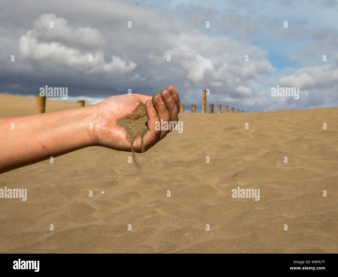 Female hand with sand against the Dunes of Maspalomas with blue sky and ...