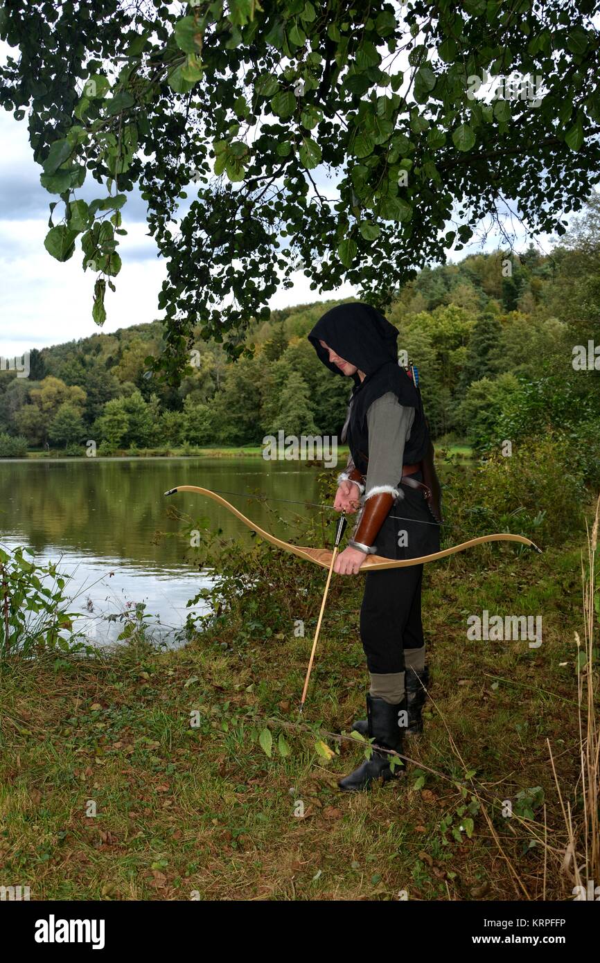 medieval archer with black hood stands with tense arch and arrow at the ...