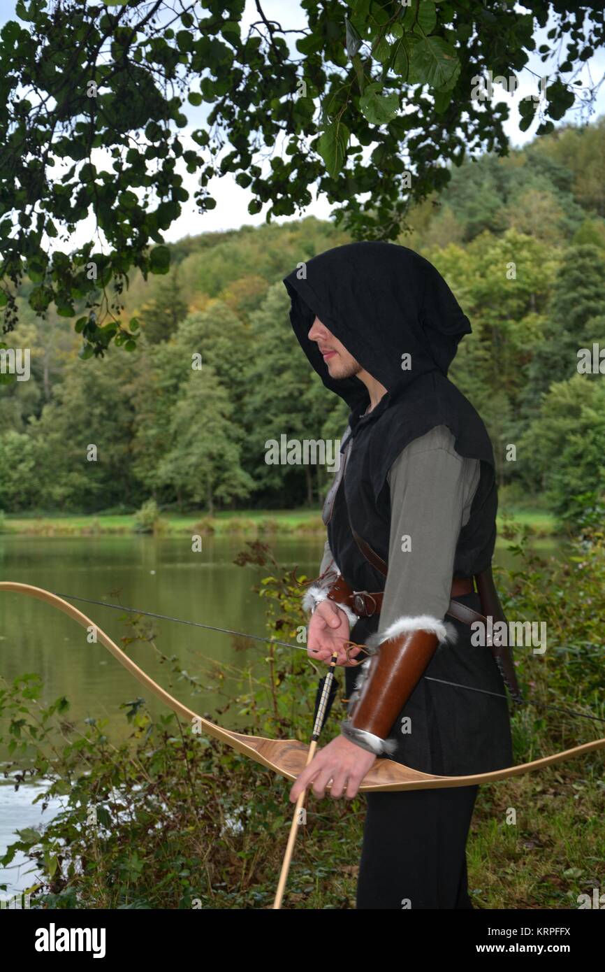 medieval archer with black hood stands with strained bow and arrow on ...