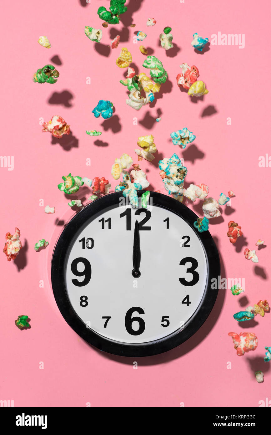 popcorn of different colors falling over a clock at twelve against a ...