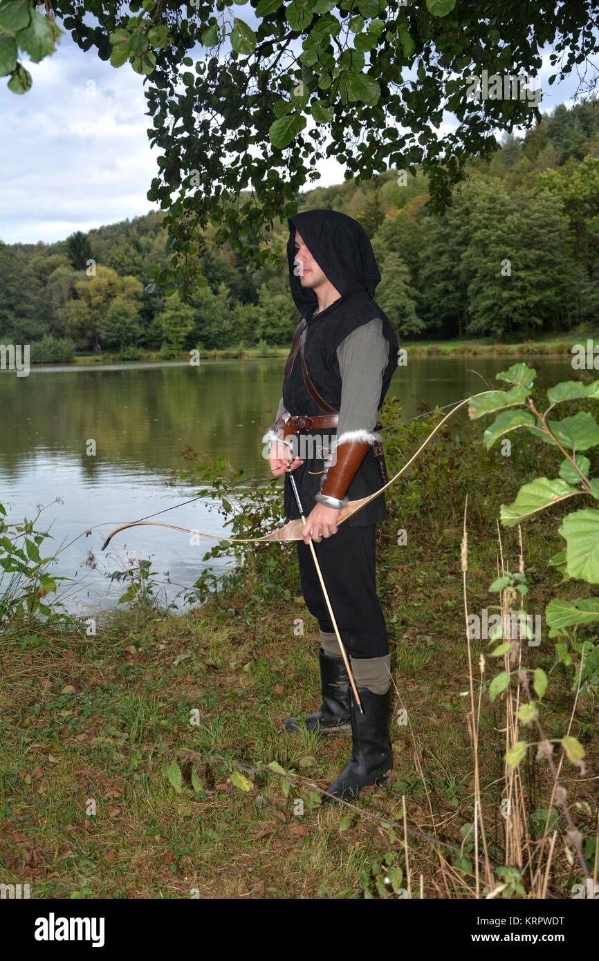 medieval archer with black hood stands with strained bow and arrow on ...