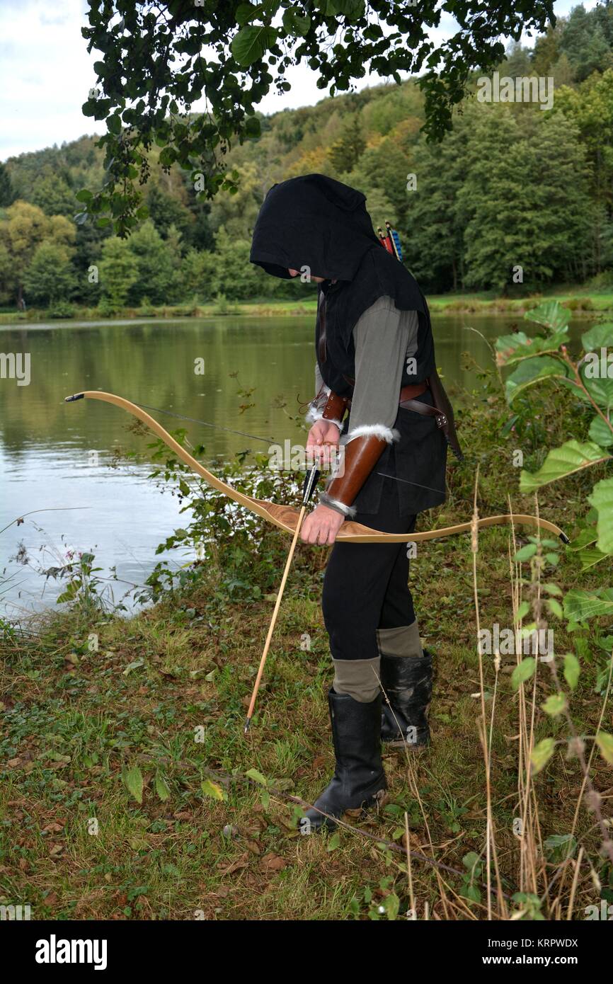 medieval archer with black hood stands with strained bow and arrow on ...