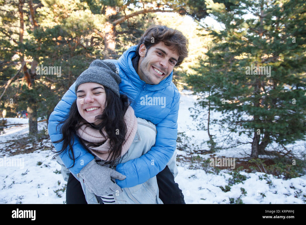 Smiling young woman carrying boyfriend on back having fun in snowy ...