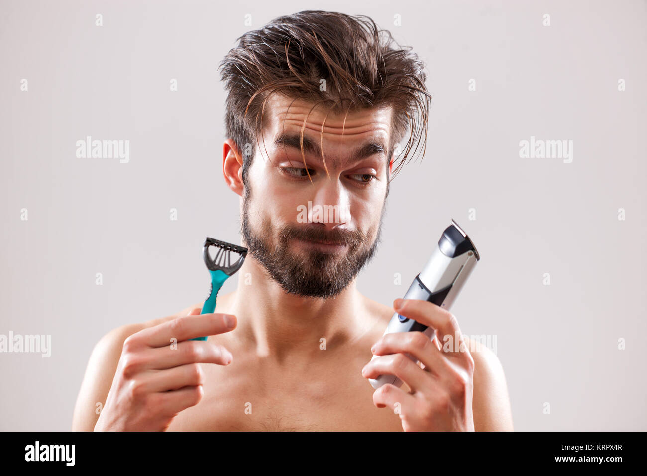 Young man is holding electric and classic razor. He is deciding which ...