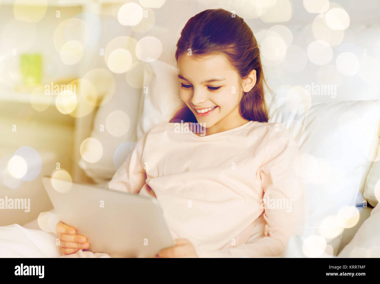 happy girl in bed with tablet pc over lights Stock Photo - Alamy