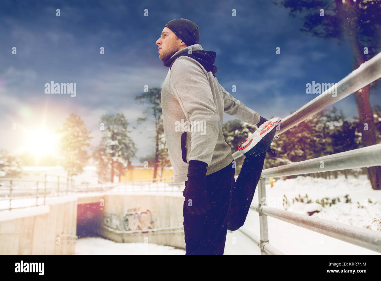 sports man stretching leg at fence in winter Stock Photo - Alamy