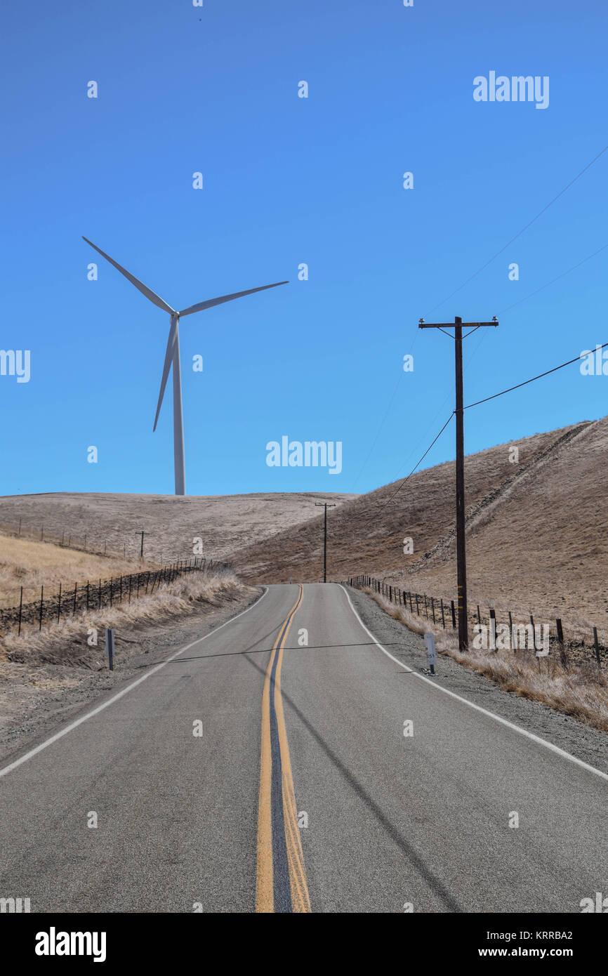 Open Road, with Two Lanes, a Wind Turbine, brown rolling hills and blue ...