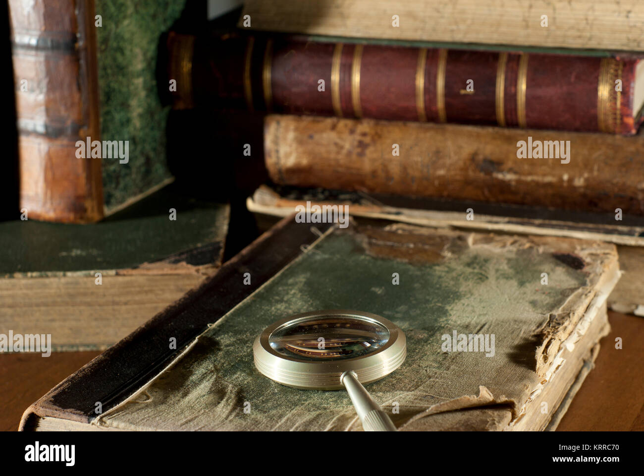 An ancient book in a ragged cover and a magnifying glass on a table ...